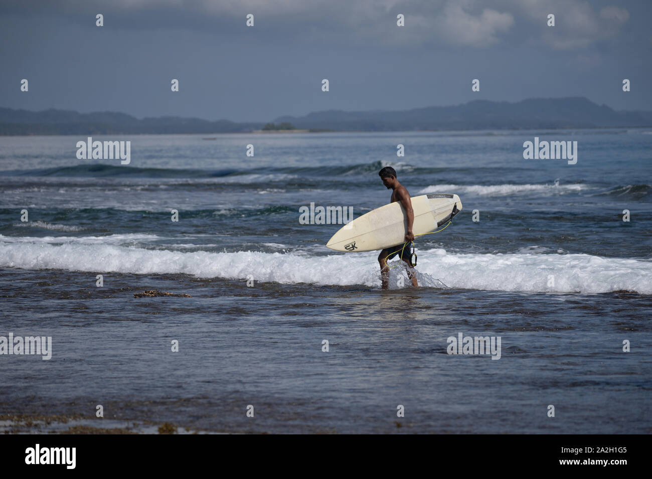 A surfer walking back to the shore after a surfing session at Cloud 9 ...