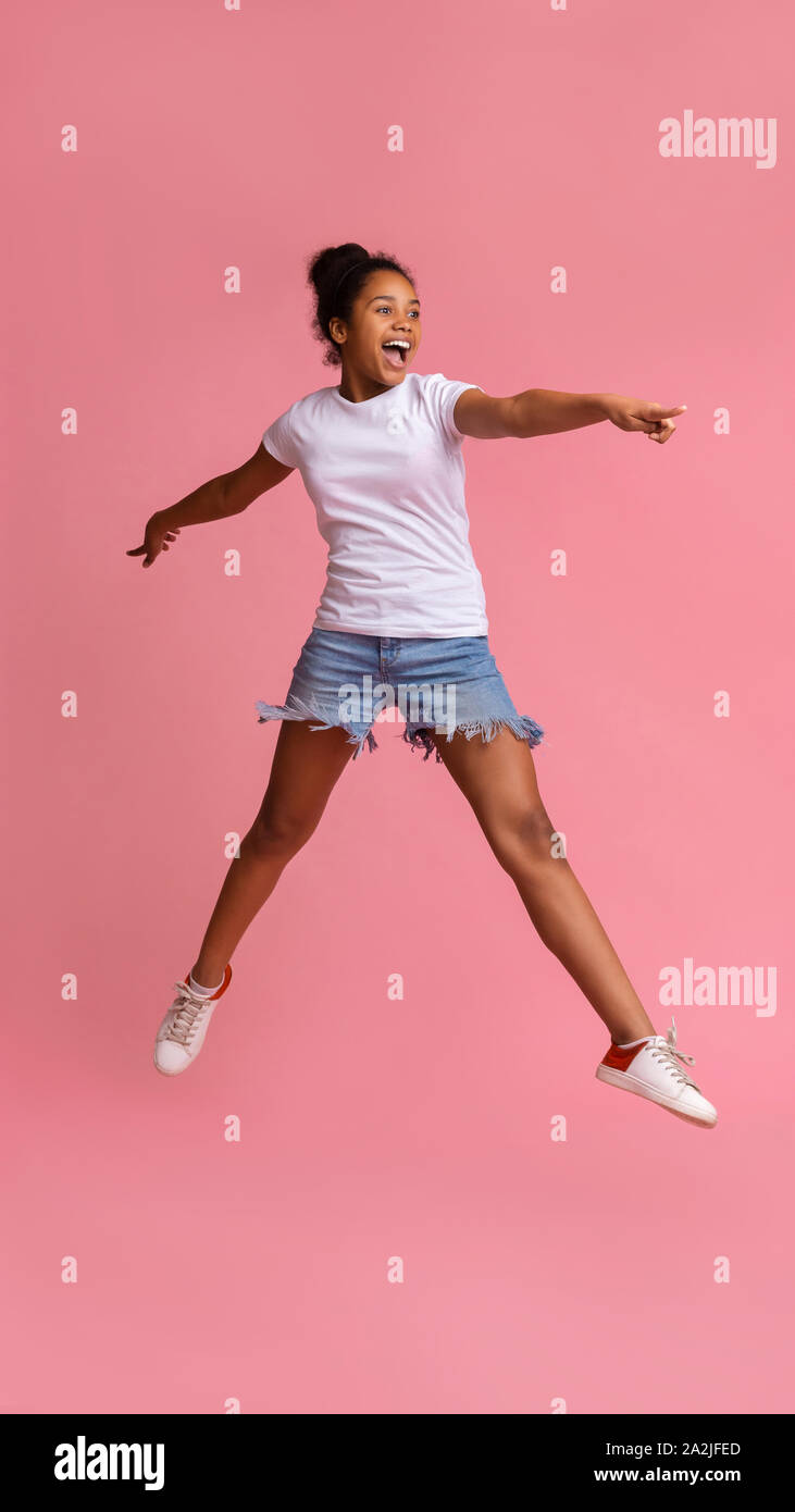 Look there. Excited african girl jumping and pointing aside Stock Photo ...