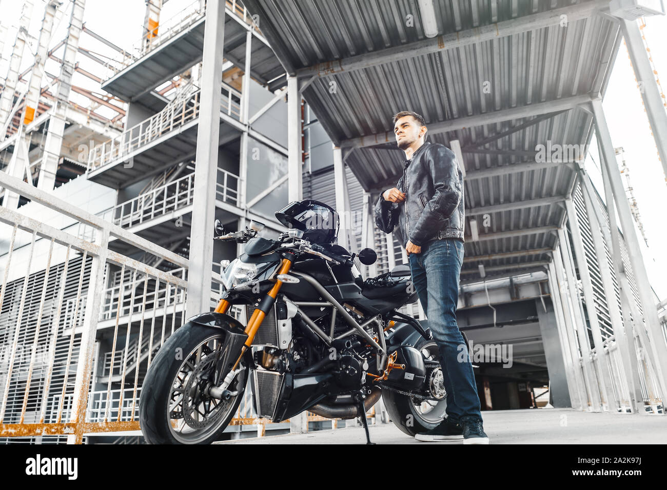 Portrait of handsome biker standing next to motorcycle on urban ...