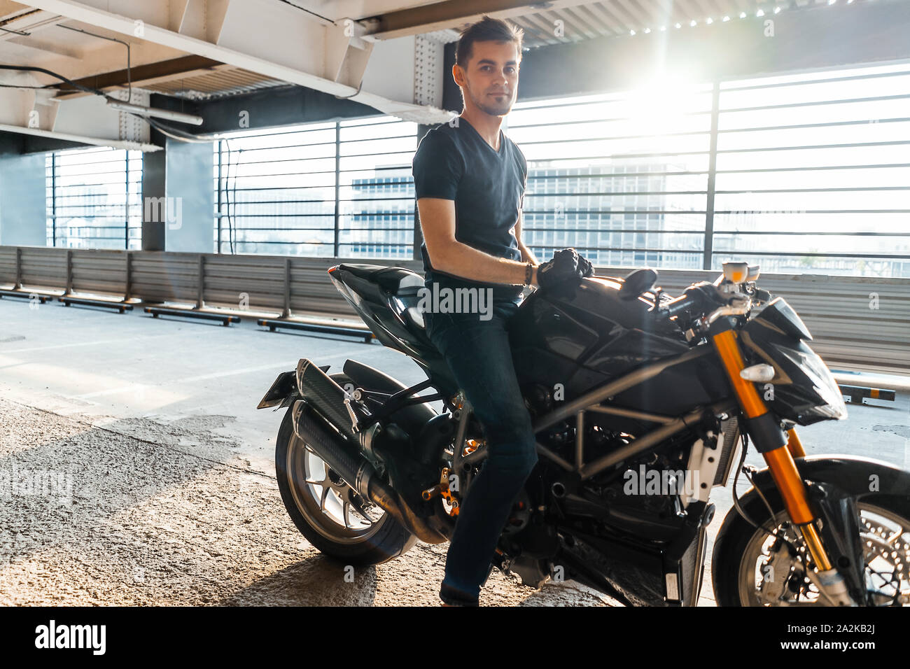 Portrait of biker riding motorcycle at parking. Urban background. Side ...