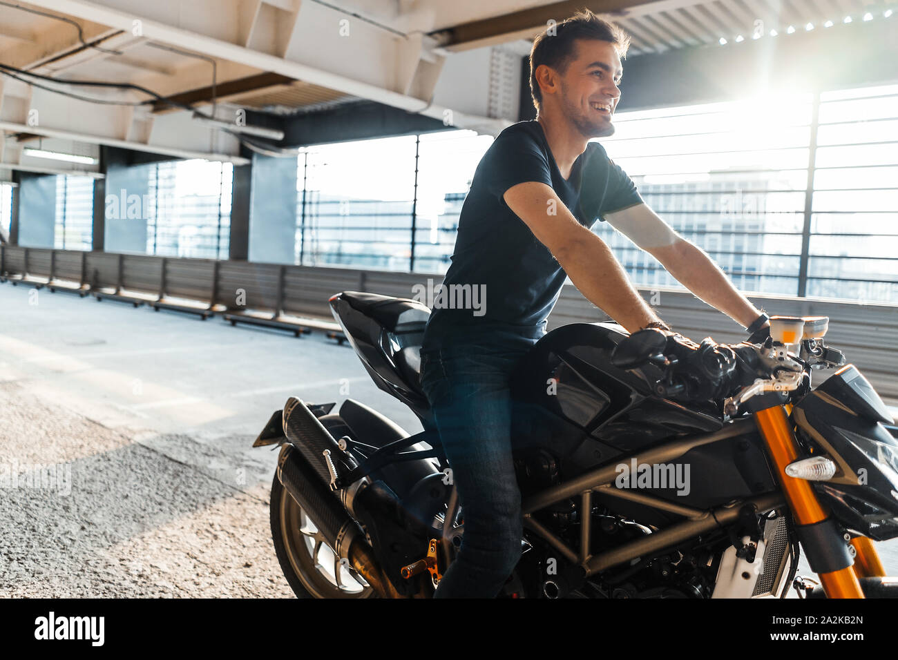 Portrait of biker riding motorcycle at parking. Urban background. Side ...