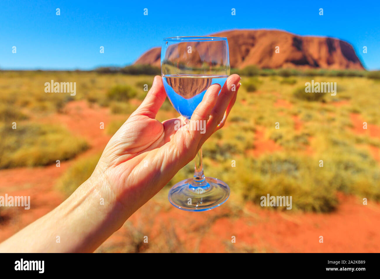 Woman's hand holding a glass goblet that reflecting Ayers Rock in Uluru ...