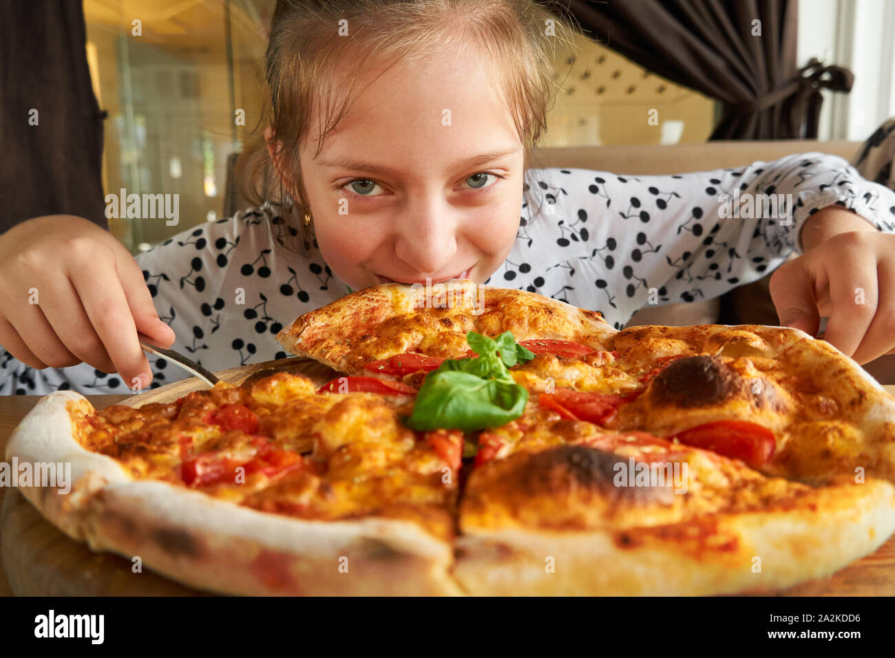 little girl eating pizza and having fun, sitting on sofa in city cafe ...