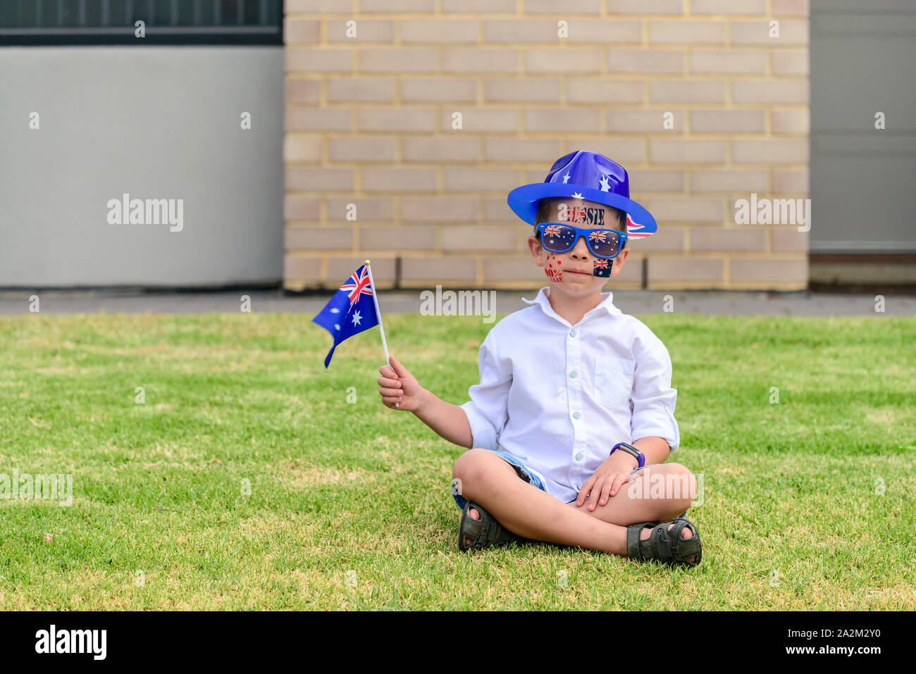 Australian boy wearing hat and sunglasses sitting on green lawn during ...