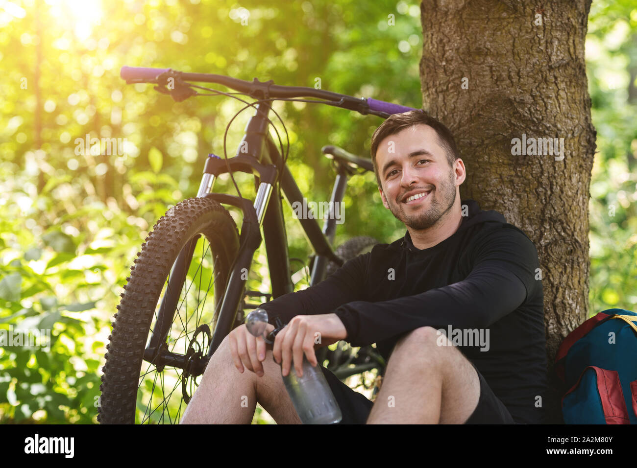 Portrait of smiling cyclist resting under tree in mountain forest Stock ...