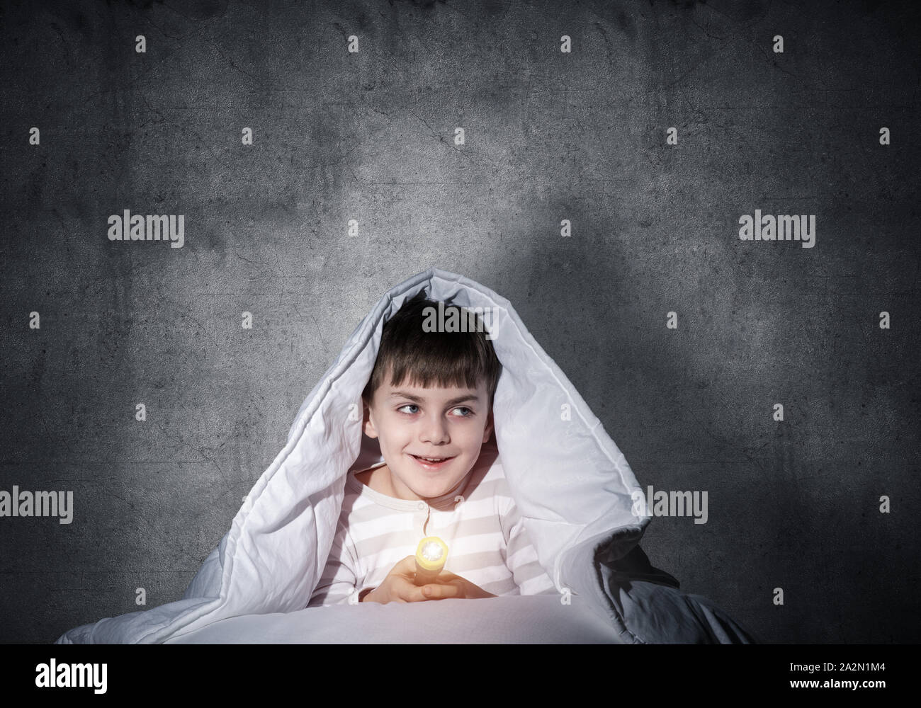 Happy child with flashlight hiding under blanket. Smiling kid lying in ...