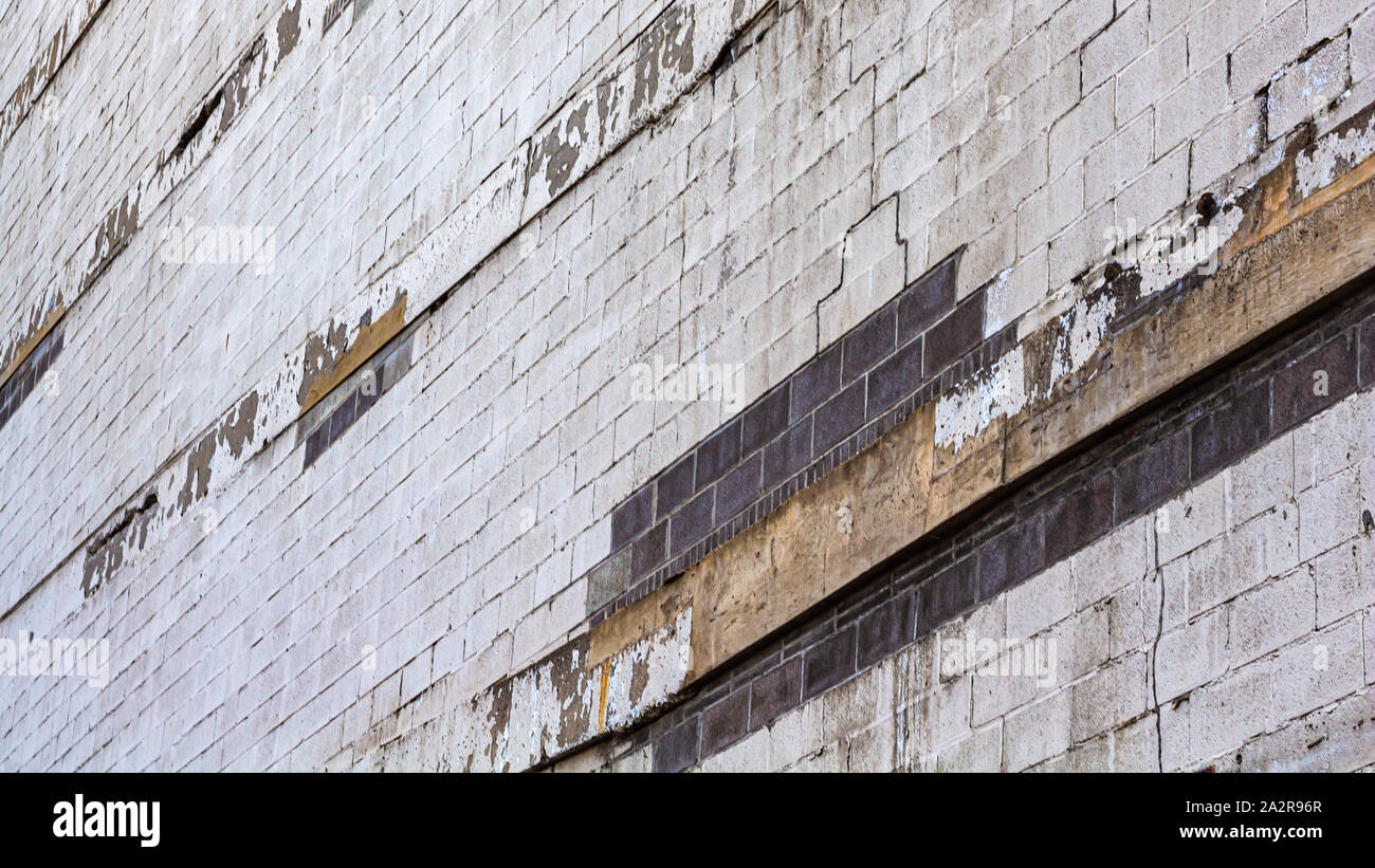 Paint is cracked, peeling and falling off an otherwise white brick wall ...