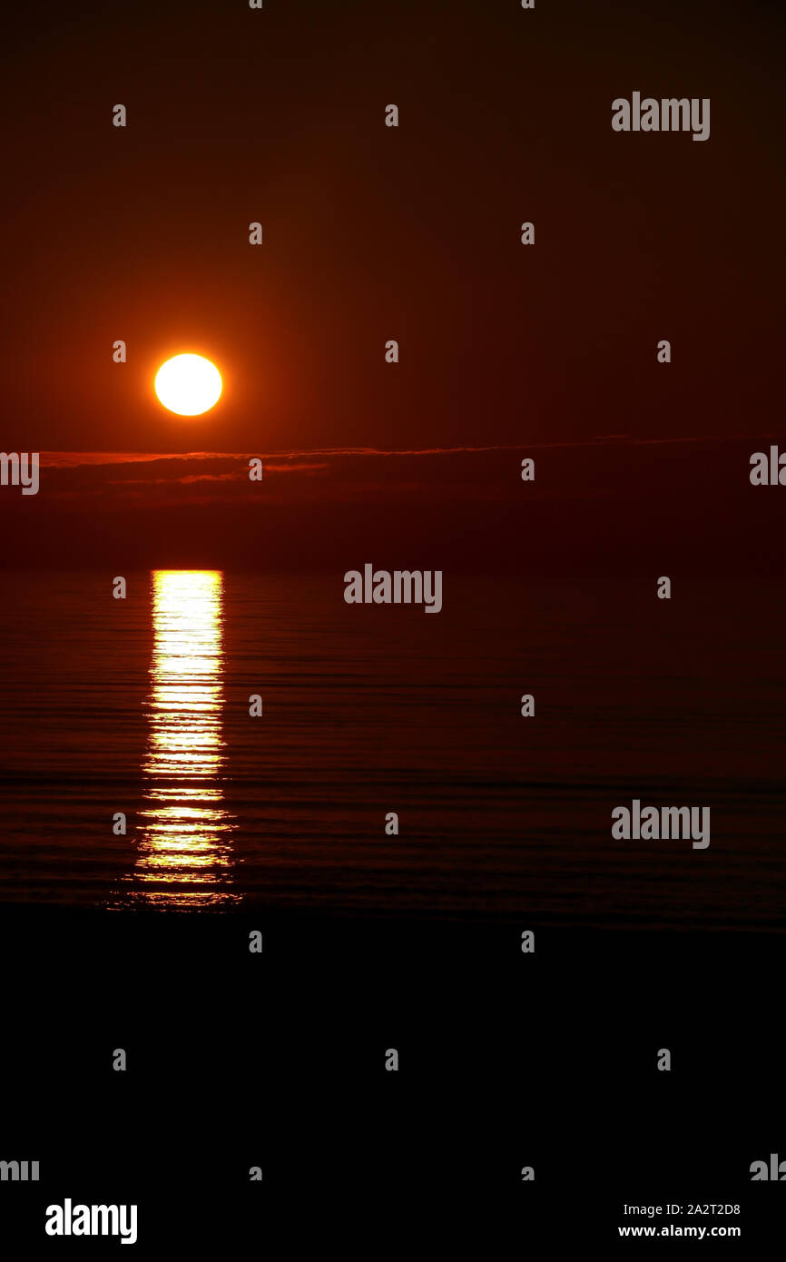 Setting sun over a coastal beach Stock Photo - Alamy