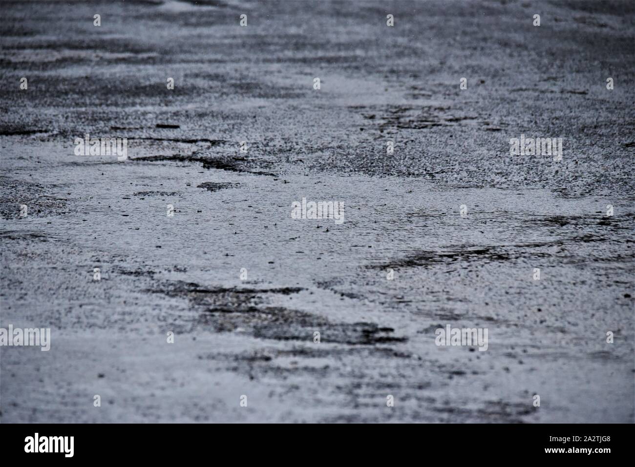 Rain falling on a road dark tarmac, with pooling water and streaming ...