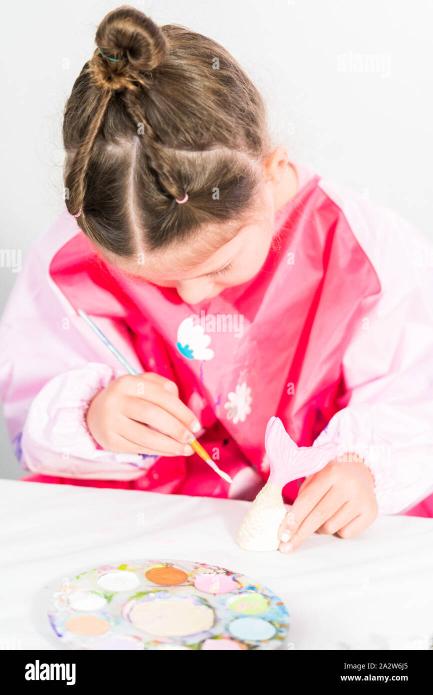 Little girl painting mermaid tails made out of modeling clay with ...