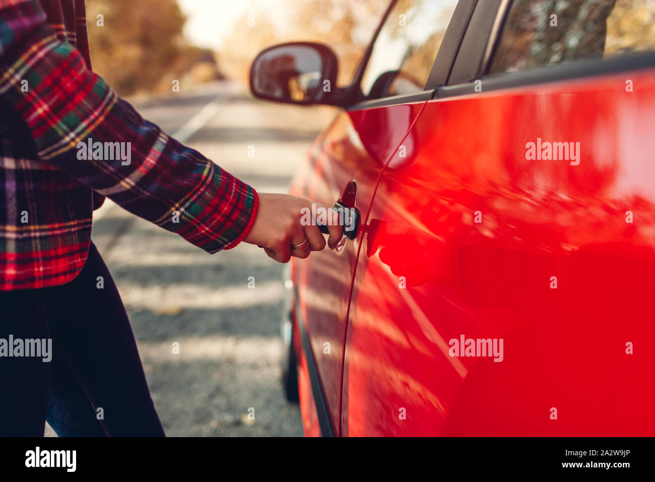 Opening car door. Woman opens red car with key on autumn road Stock ...