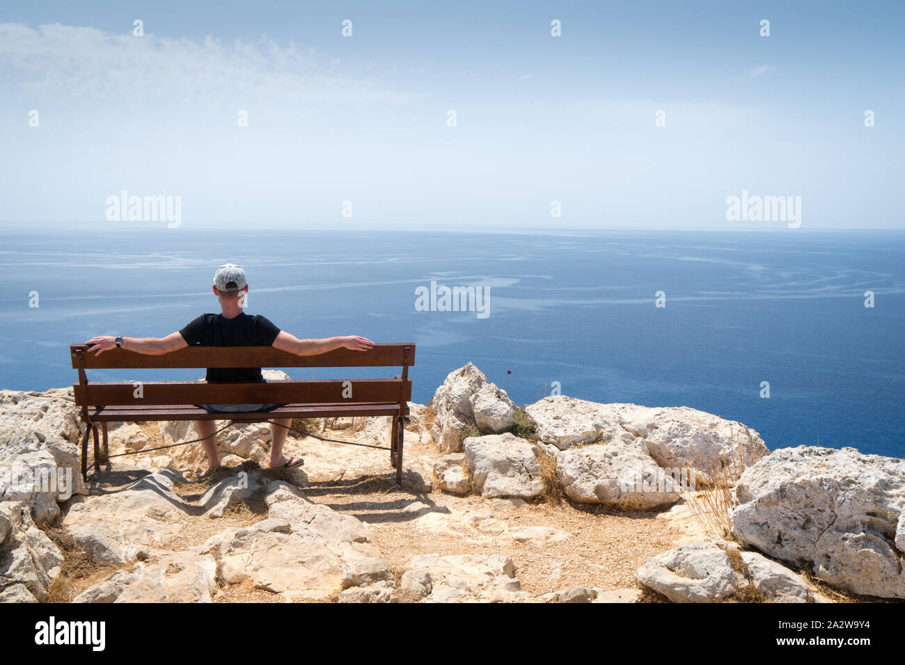 Guy sitting on wooden bench and looking at the blue ocean in Ayia Napa ...