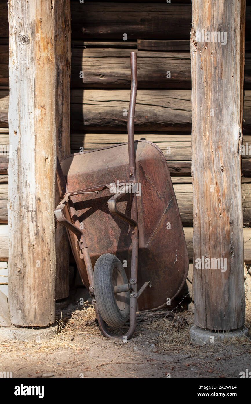 Old vintage wheelbarrow leaning on a log cabin wall Stock Photo - Alamy