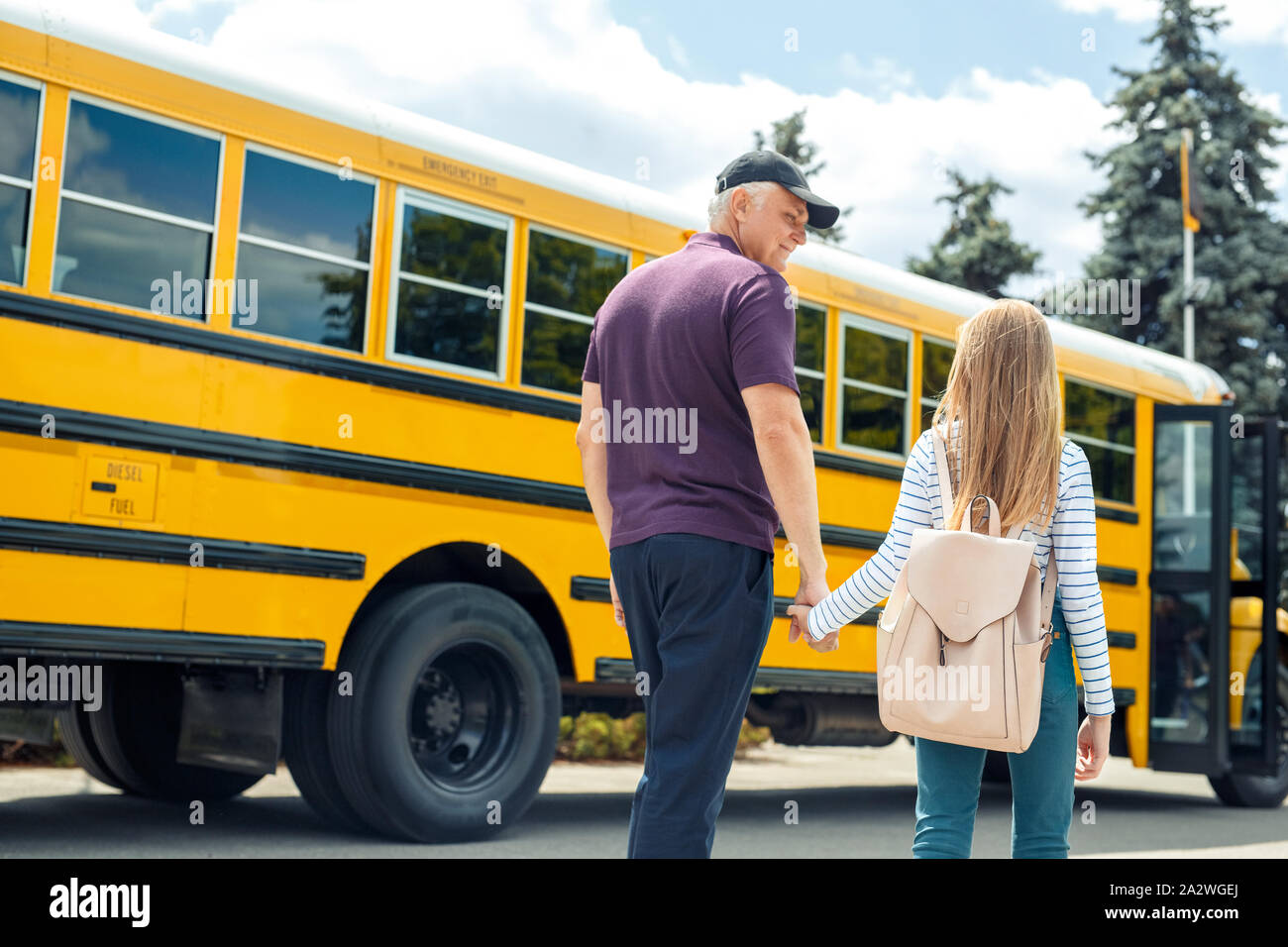 Father and daughter holding hands walking to school bus smiling relaxed ...