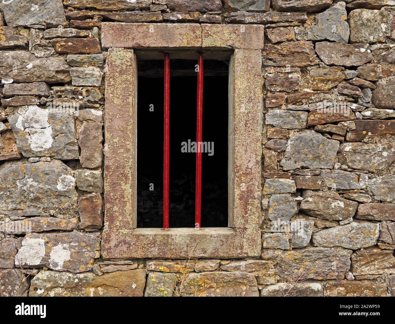 2 vertical red iron bars across sandstone bordered window of stone barn ...