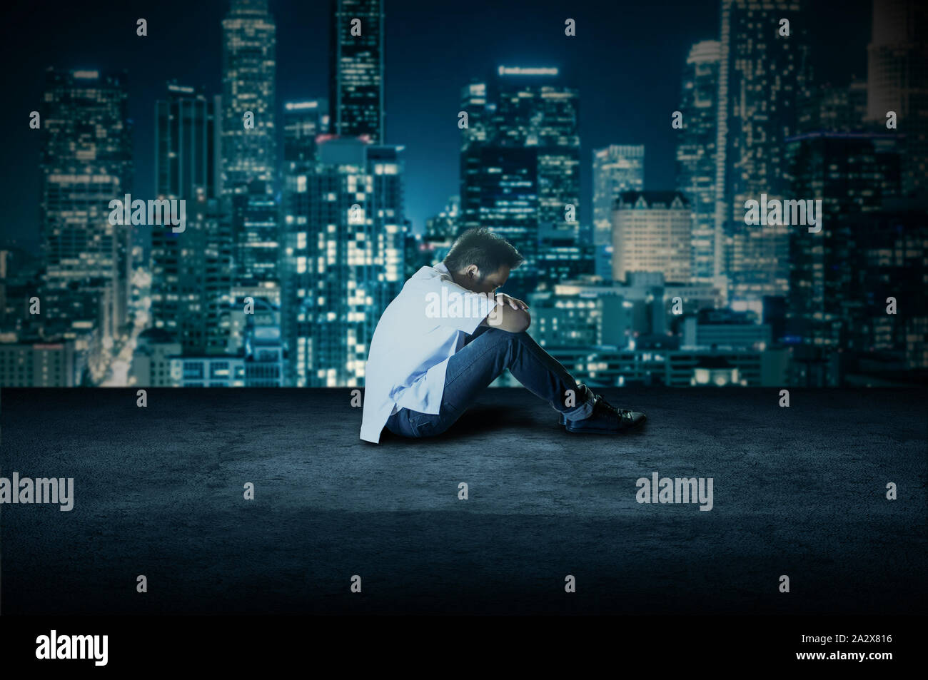 Wide shot of a young man sitting and crying on a floor of the roof top ...
