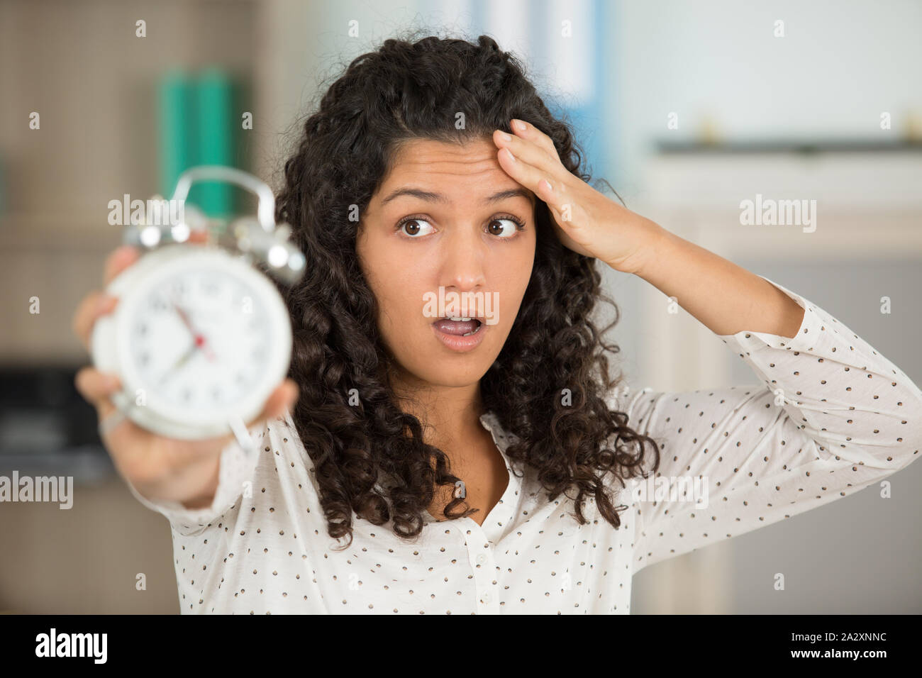young woman looking terrified holding an alarm clock Stock Photo - Alamy