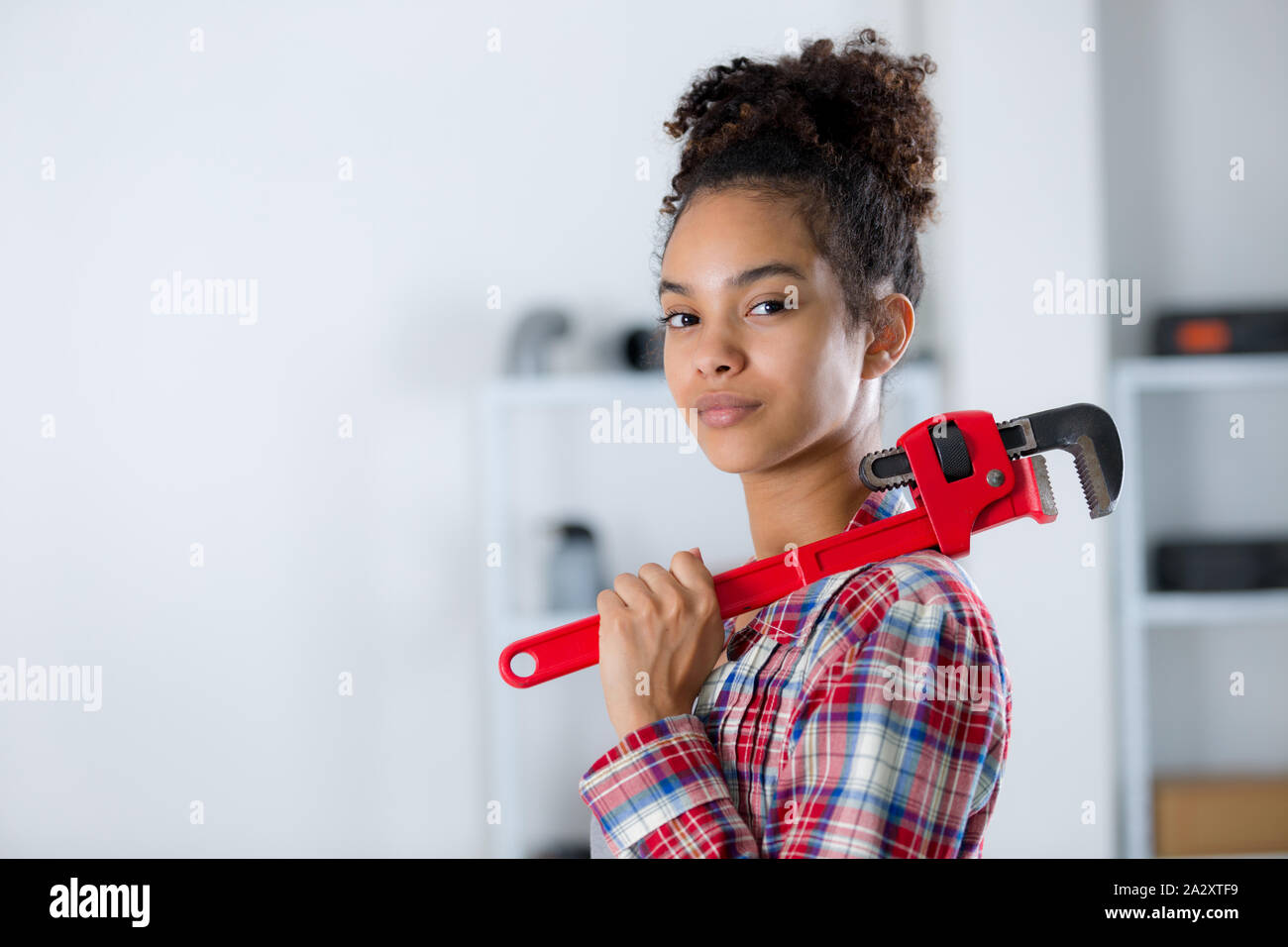 confident young woman carrying adjustable wrench over her shoulder ...