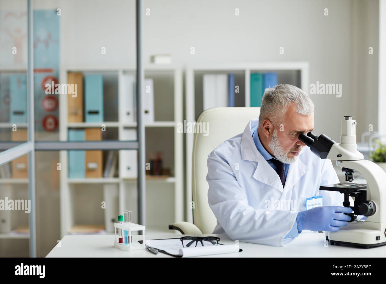 Senior doctor sitting at his workplace and examining samples through ...
