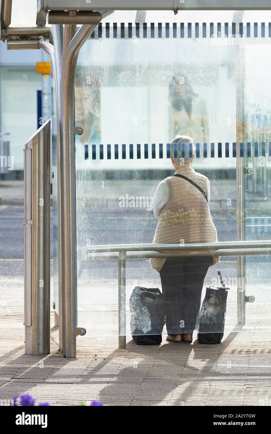 A woman with her two shopping bags waits at a bus stop in the town ...