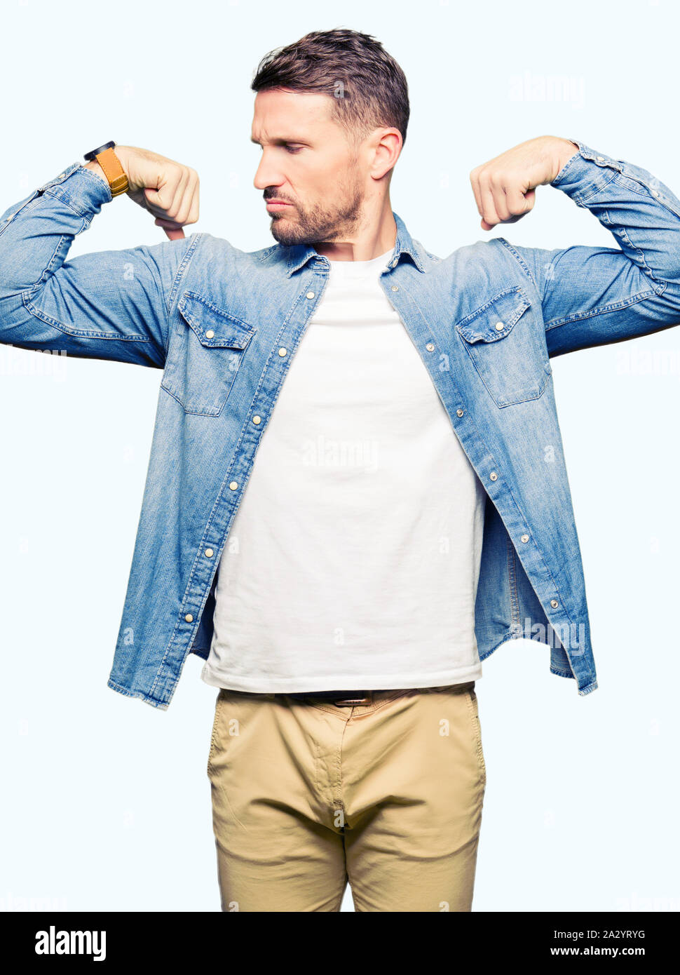 Handsome man with blue eyes and beard wearing denim jacket showing arms ...