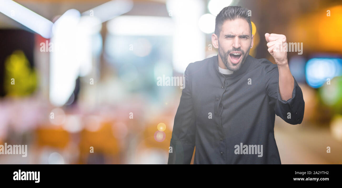 Young Christian priest over isolated background angry and mad raising ...