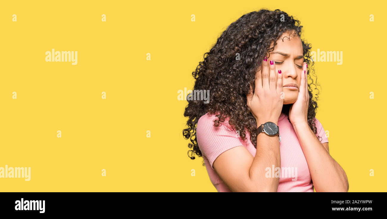 Young beautiful woman with curly hair wearing pink t-shirt with sad ...
