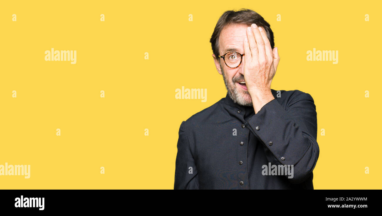 Middle age priest man wearing catholic robe covering one eye with hand ...
