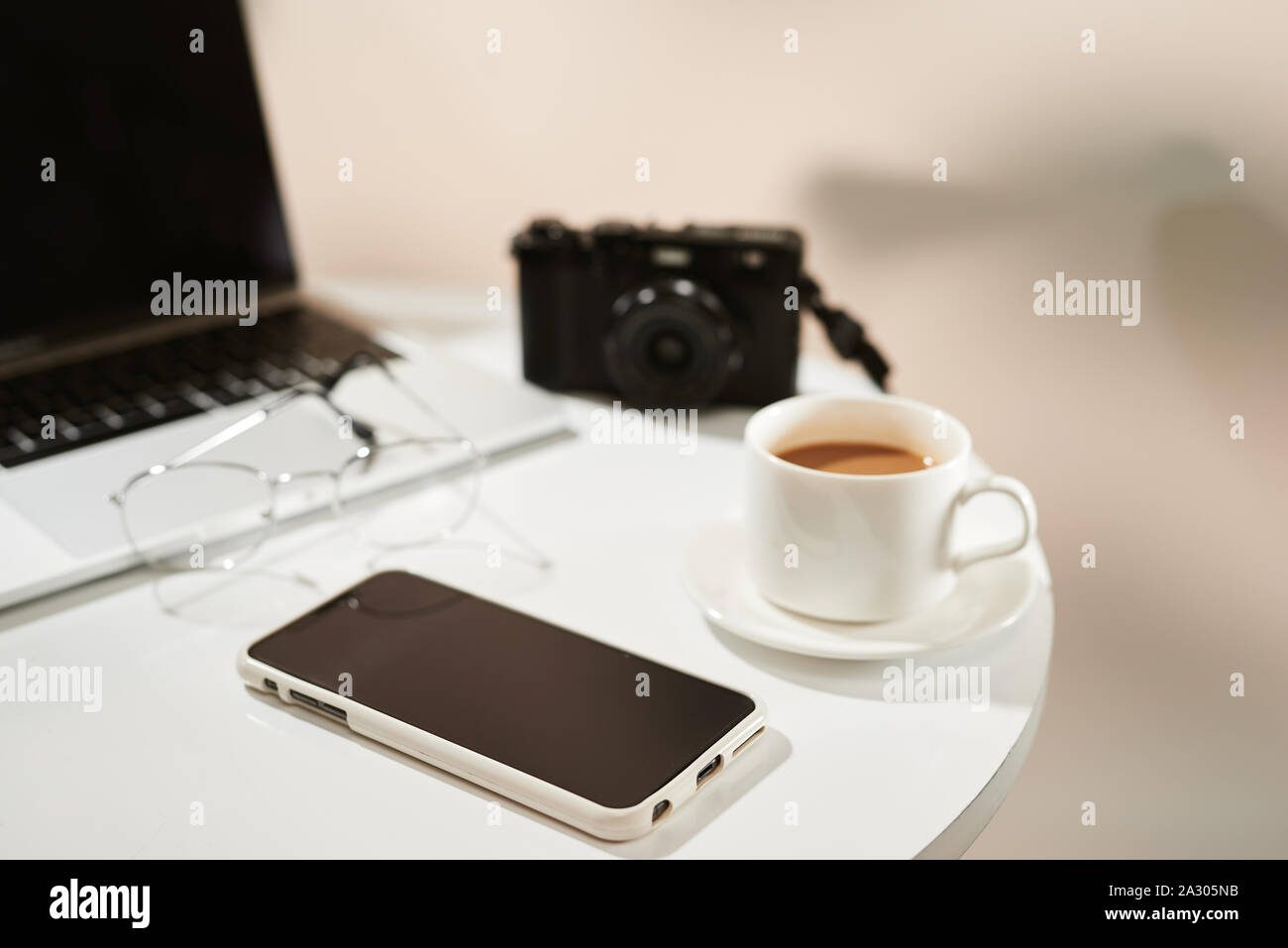 Office desk with mobile phone, coffee cup, laptop, camera and glasses ...
