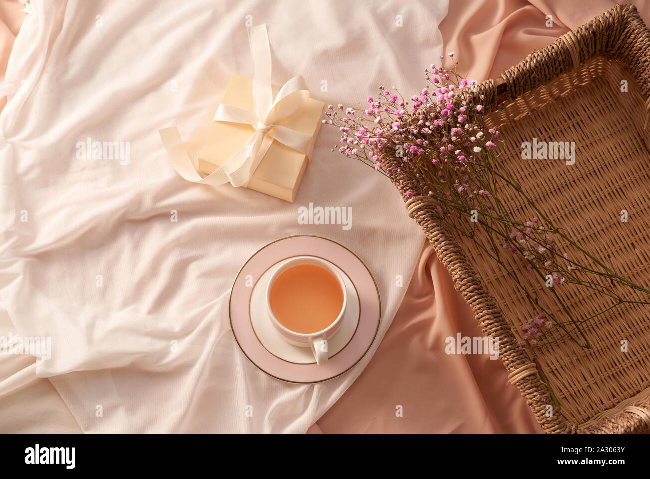 Cup of tea, gift box and flowers on tray on light fabric background ...