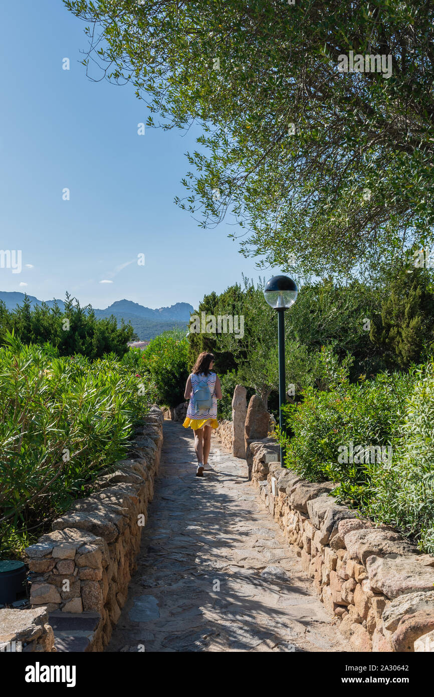 European woman in dress back view walking down a narrow alley against a ...