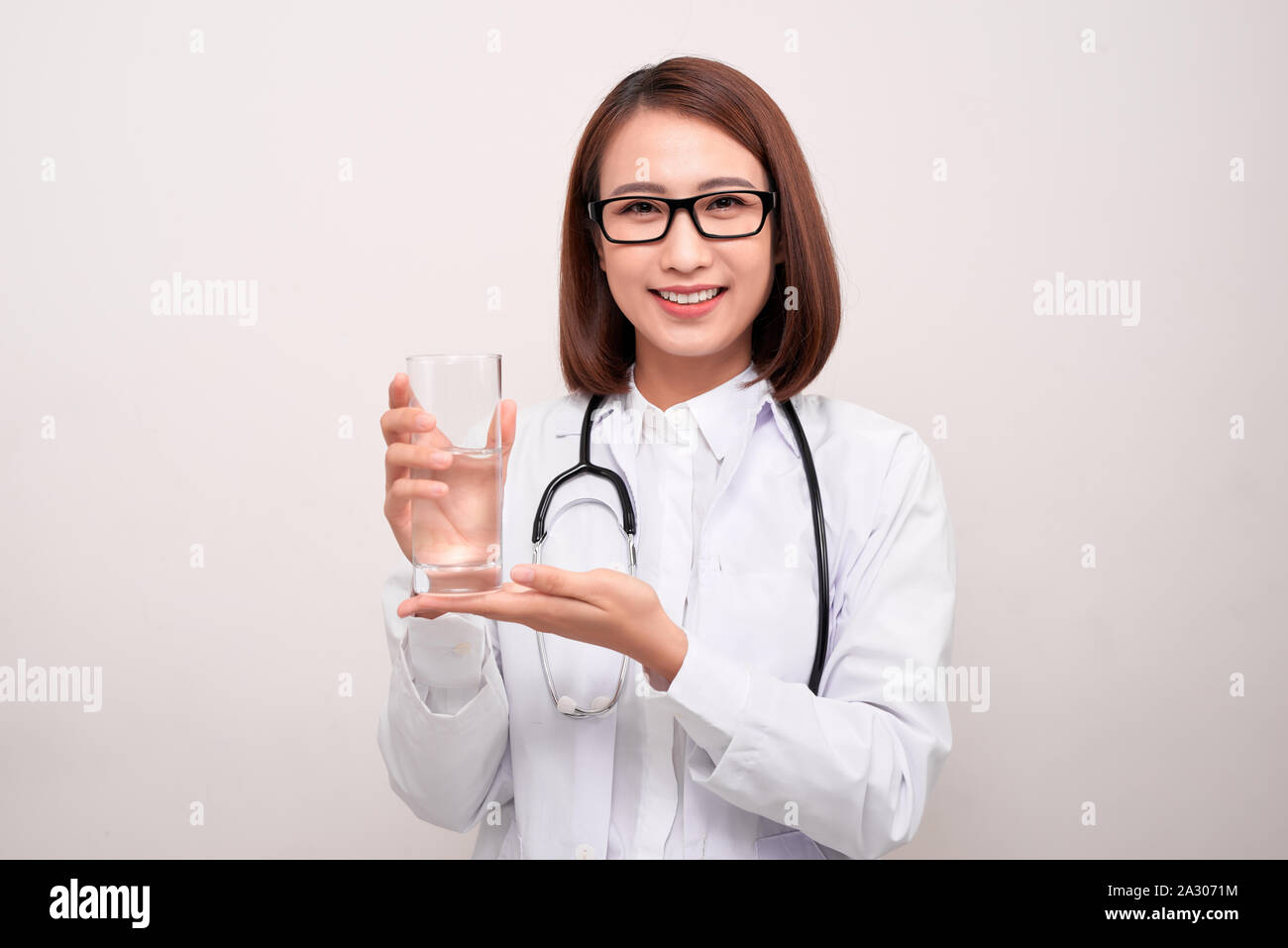 young woman doctor standing and holding glass of water over white ...