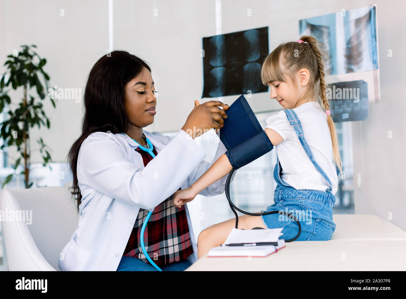 Little girl visiting young female African doctor in hospital. Measuring ...