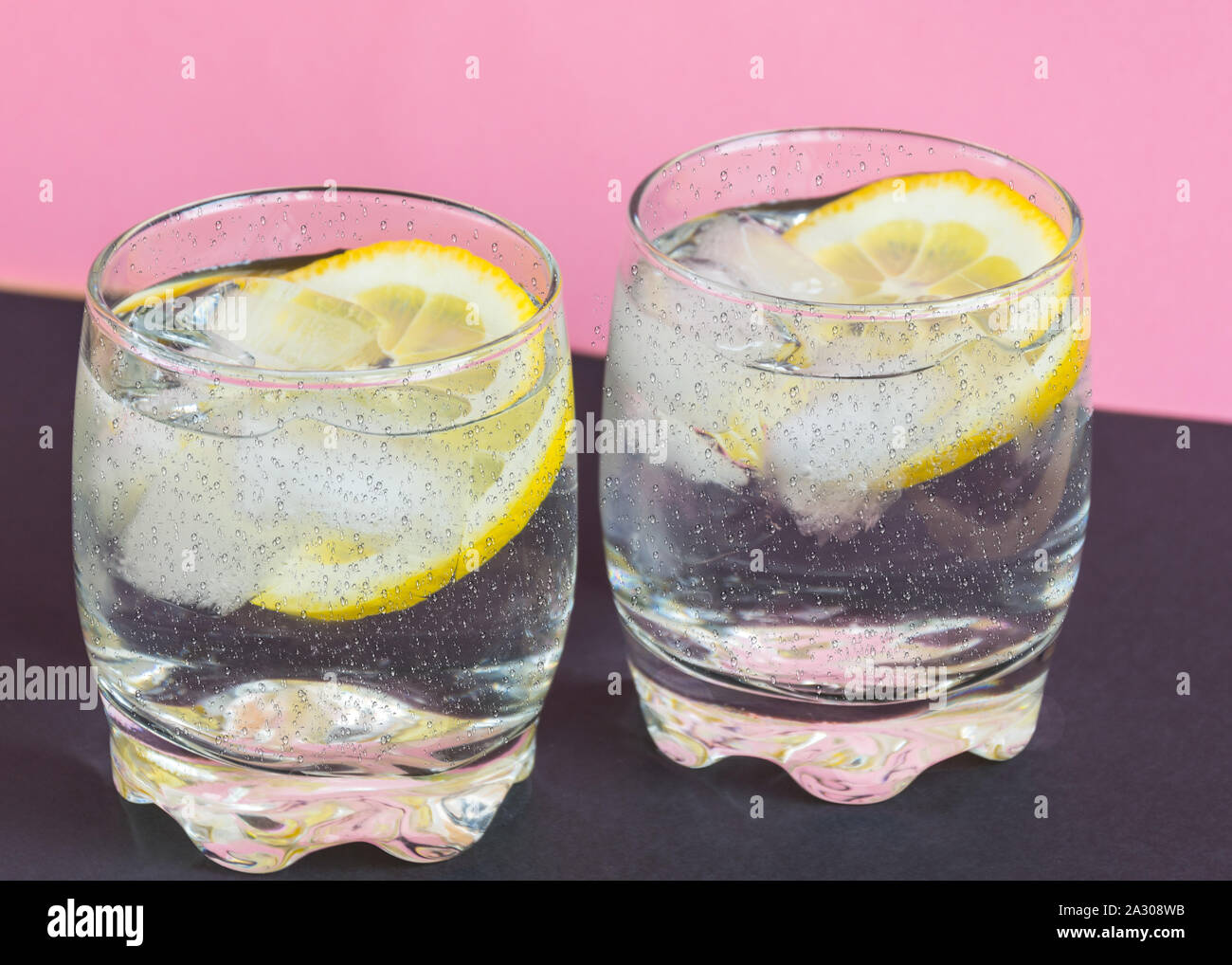 Two glasses of fresh cold water with lemon slices and ice on pastel ...