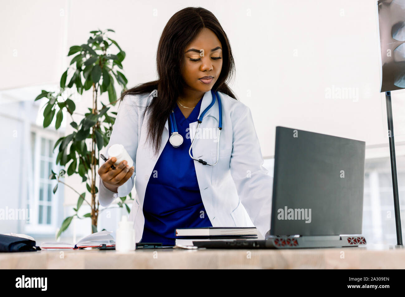 Black female doctor at work in an office, looking to laptop. Beautiful ...