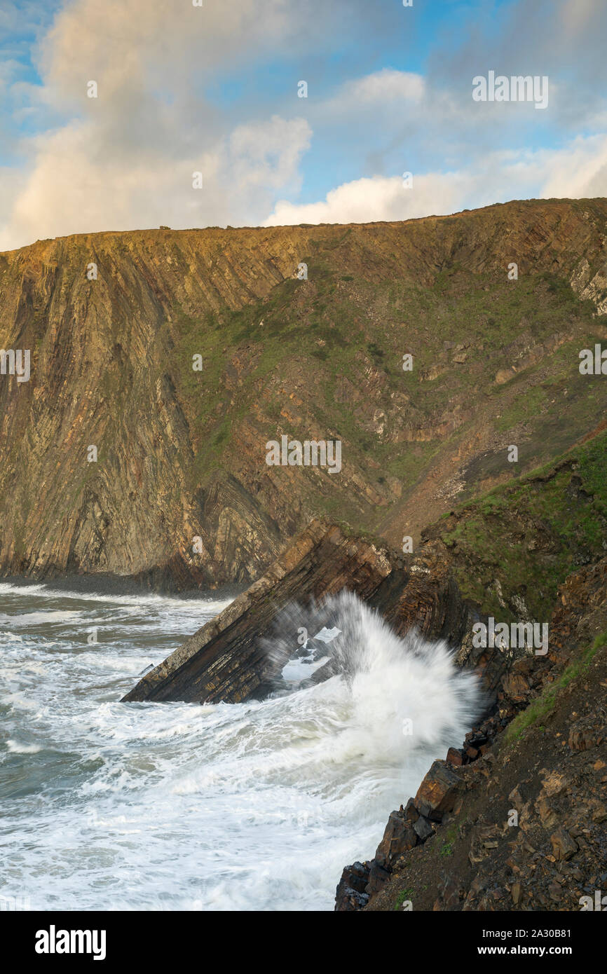 Waves crash over a natural stone arch below the cliffs of hartland ...