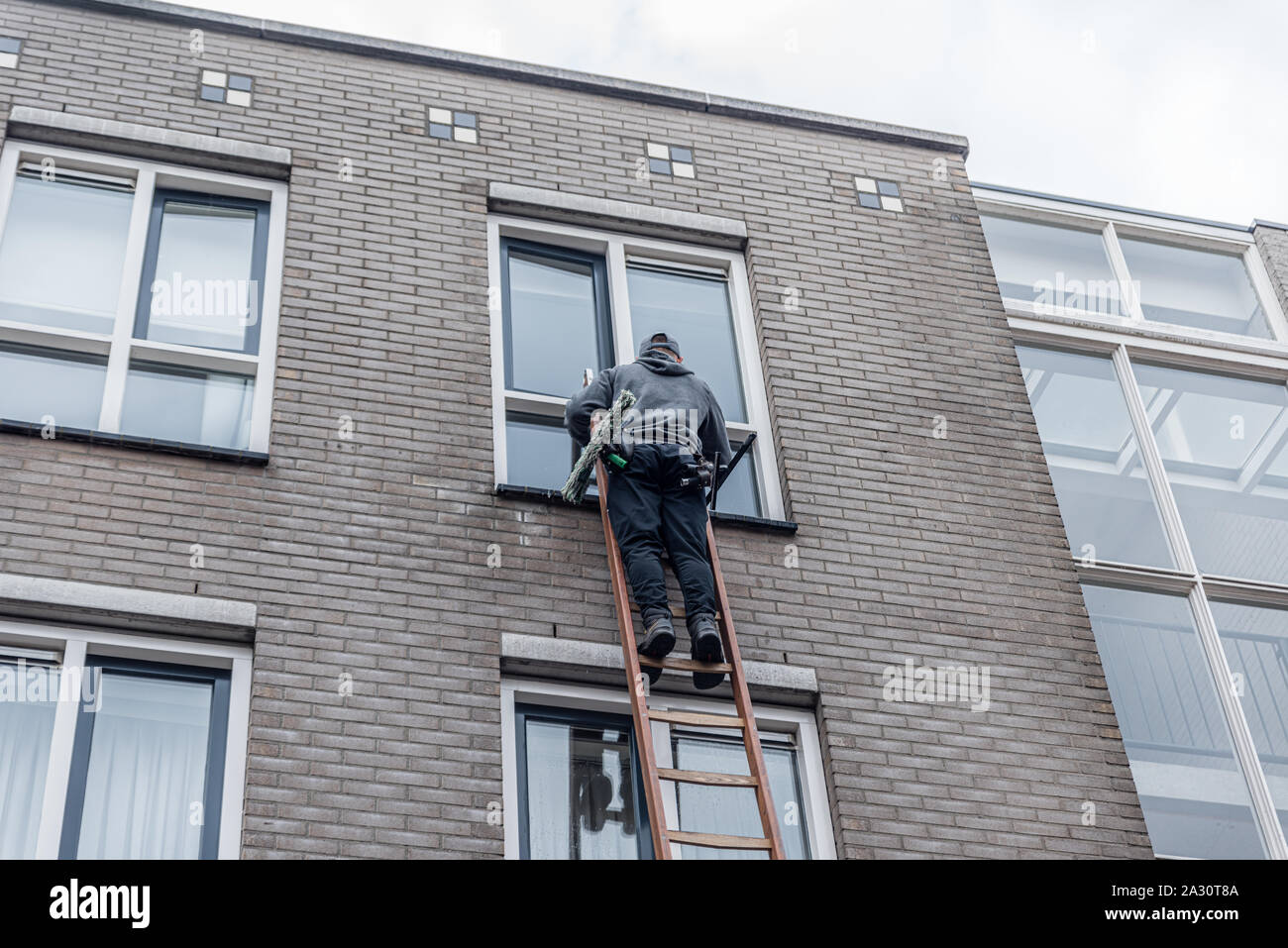 Window cleaner on a ladder cleaning the windows high against a building ...