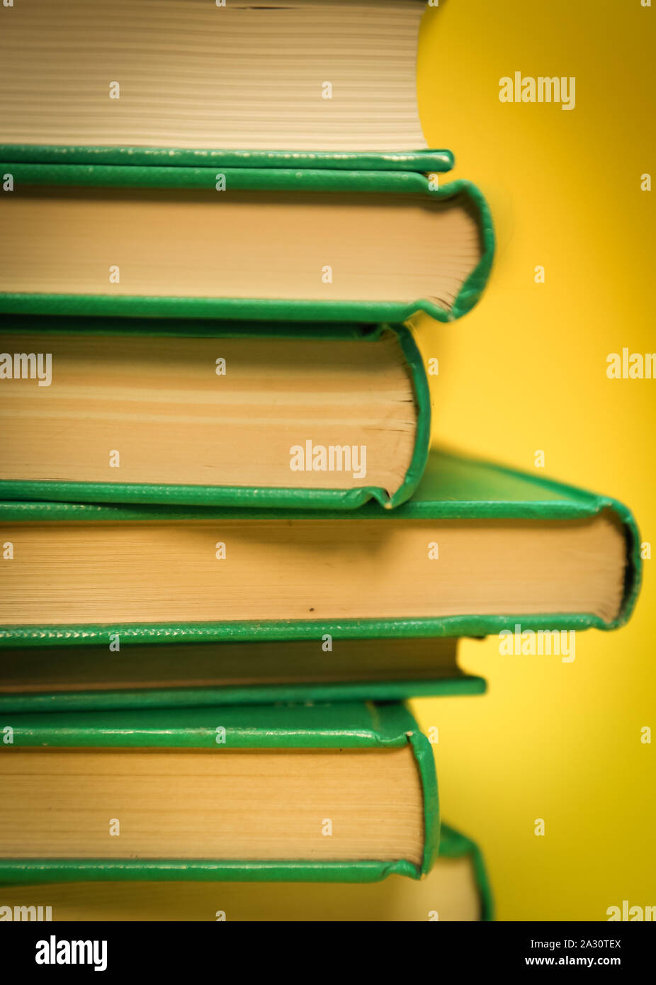 crop of a vertical stack of books. Yellow background and green books ...