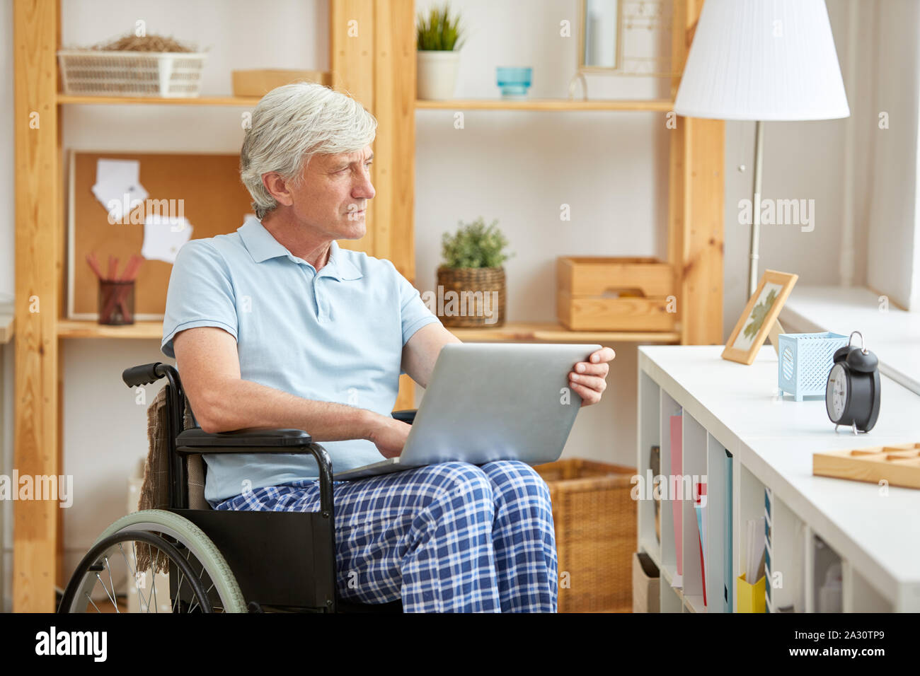 Senior disabled man in wheelchair looking out the window while using ...