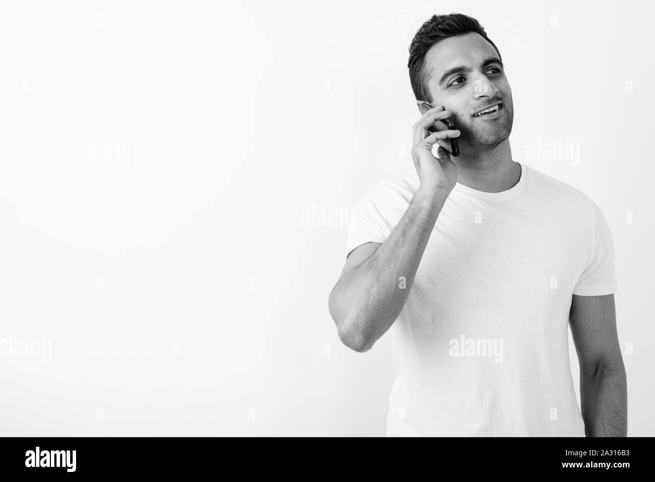 Young handsome Indian man using mobile phone against white background ...