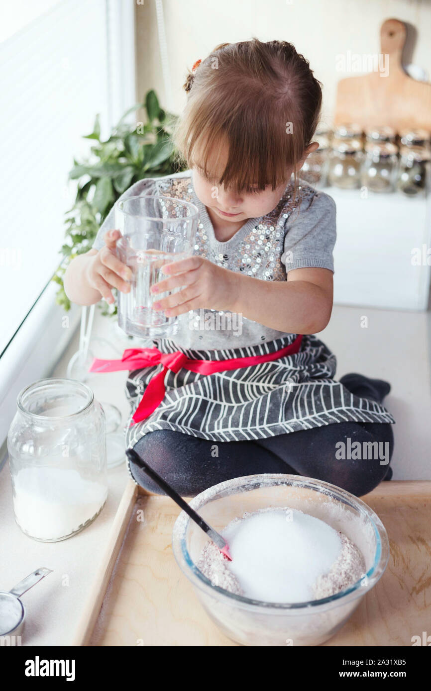 3-year-old girl and her mother measuring dry ingredients for baking ...