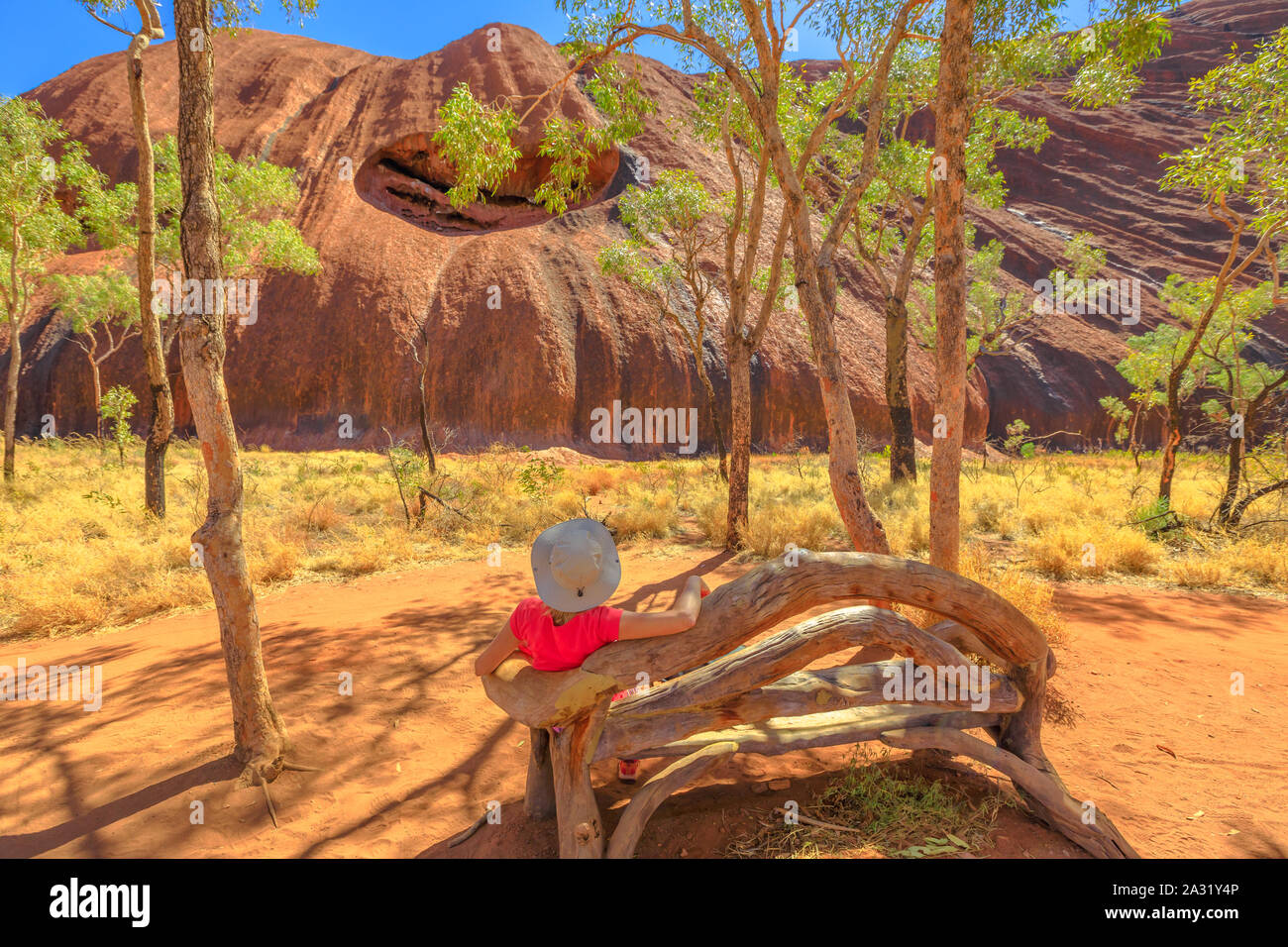 Tourist woman with wide hat rest on wooden bench along Uluru Base walk ...