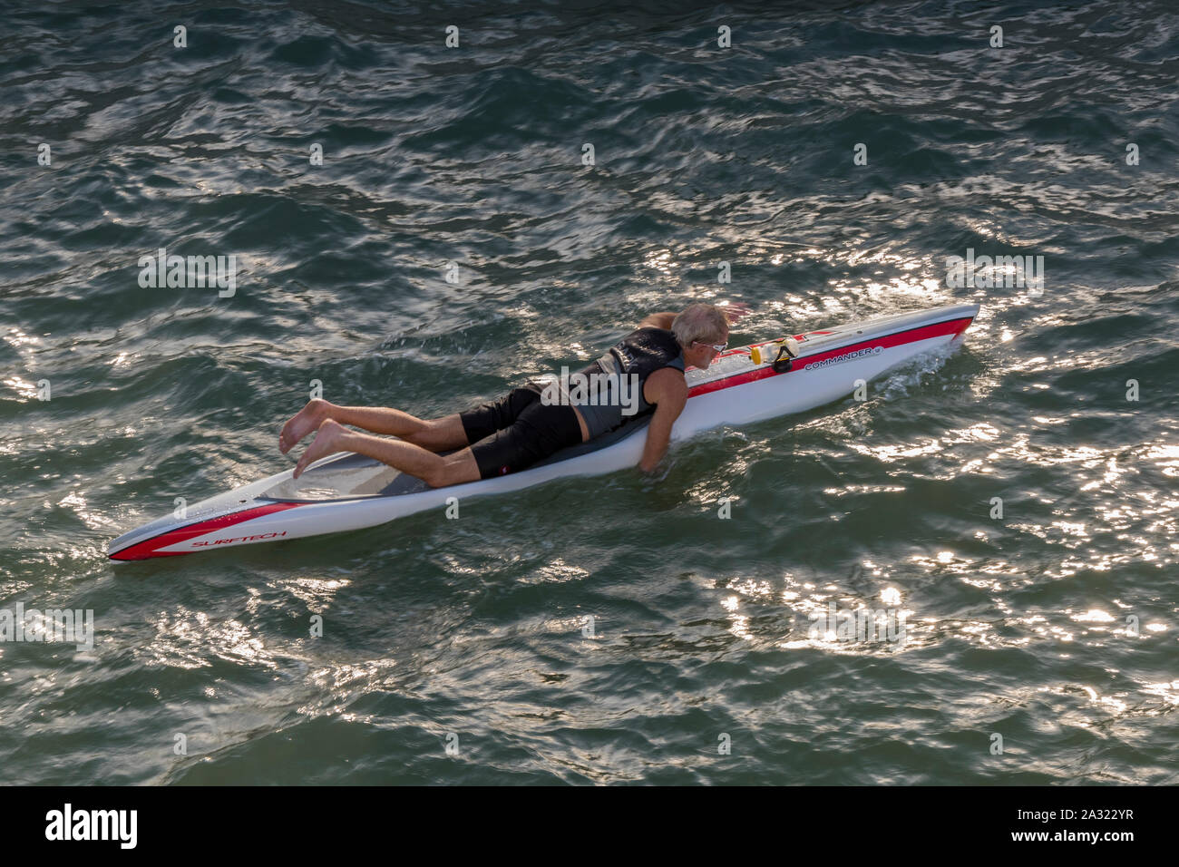 a man lying on a surfboard paddling with his hands on the sea afloat ...