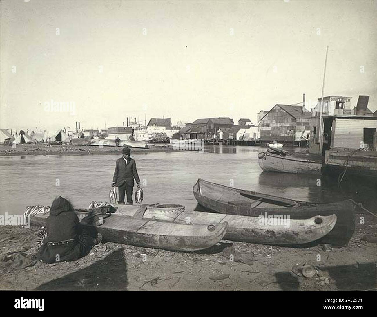 Eskimo man and woman preparing fish next to kayaks on the beach Snake ...