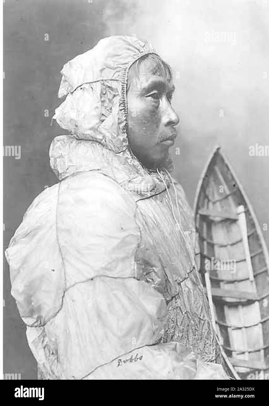 Eskimo man wearing rain gear and holding model of umiak Alaska between ...