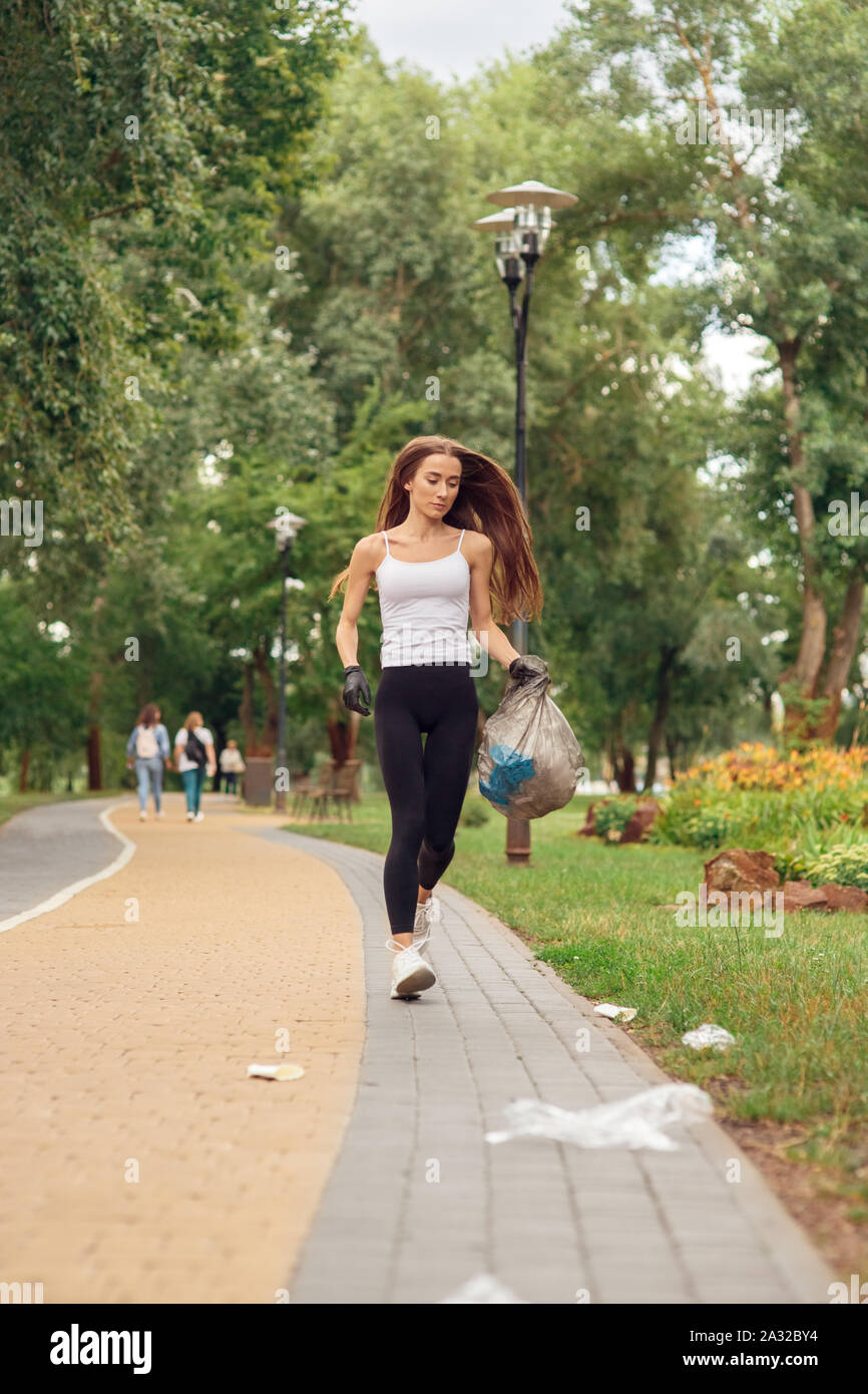 Plogging. Young girl volunteer running concentrated outdoors picking up ...