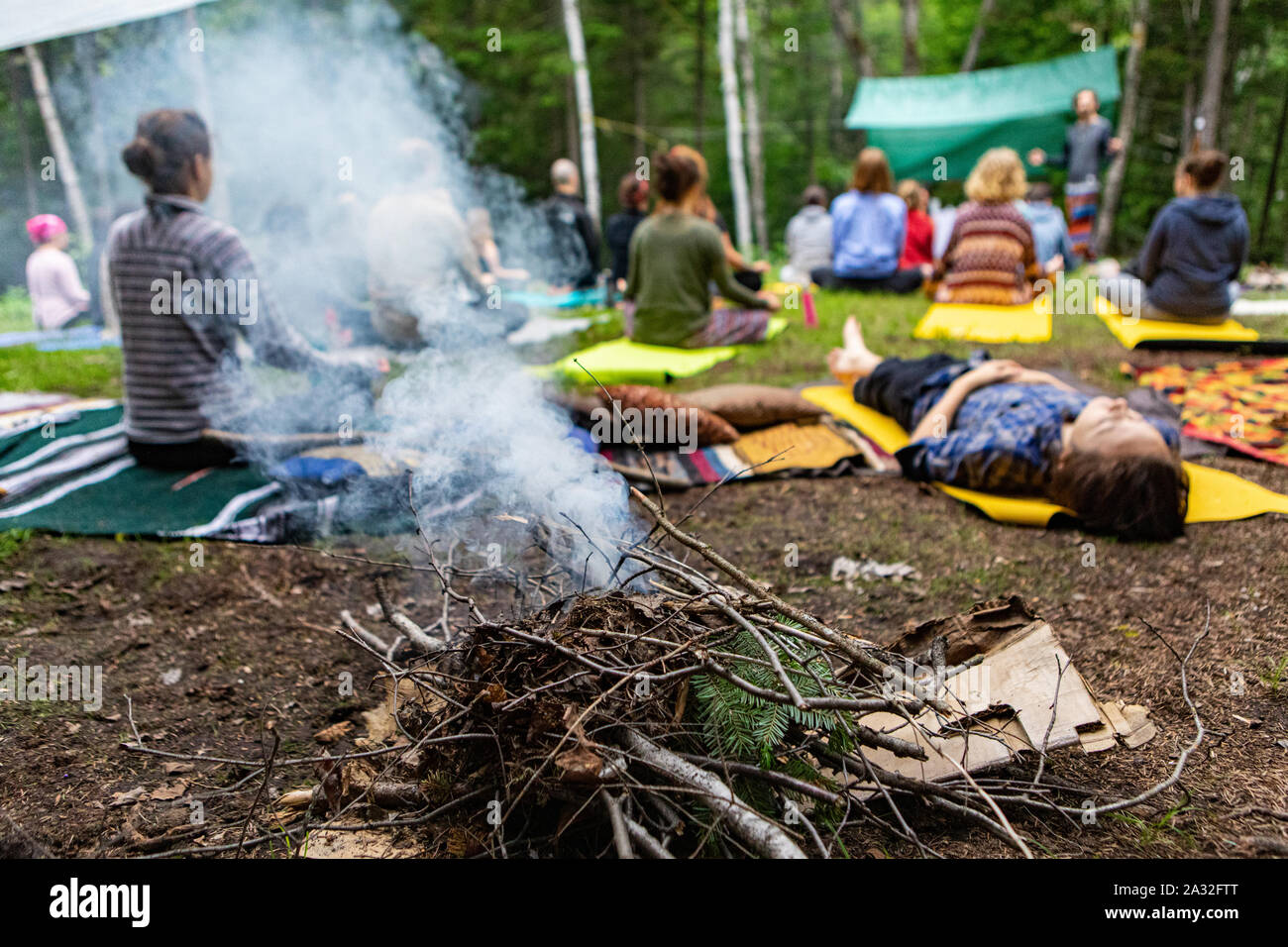 A close up view of campfire kindling smoking as blurred people are seen ...