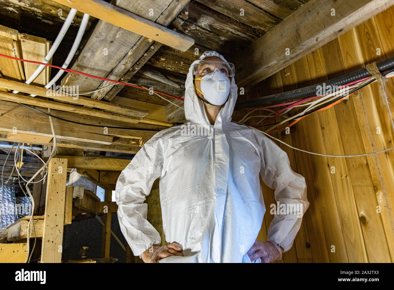A close up view of a man standing indoors wearing hooded boiler suit ...