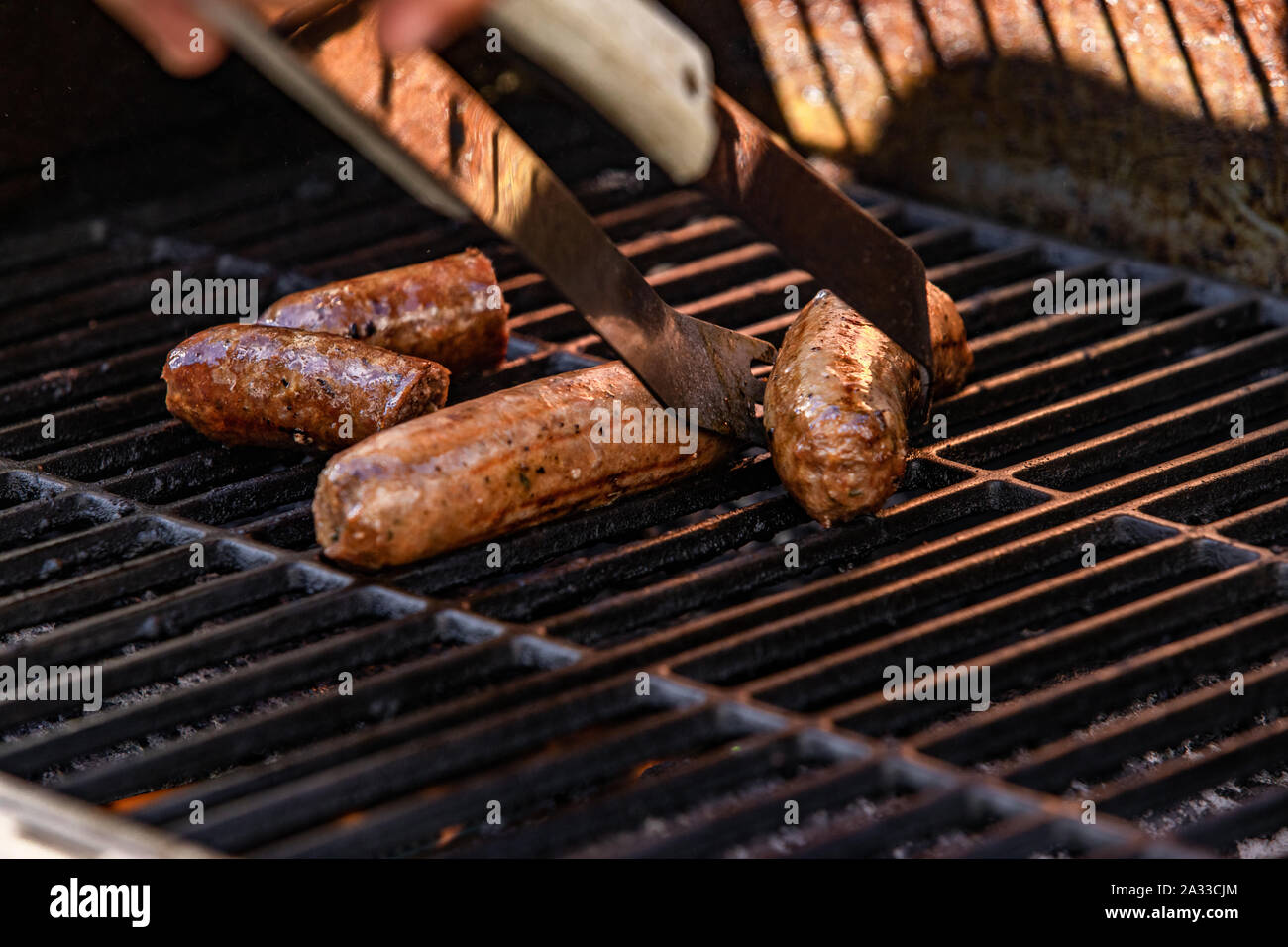 Golden brown sausages are seen closeup, cooking on an outdoor barbecue ...