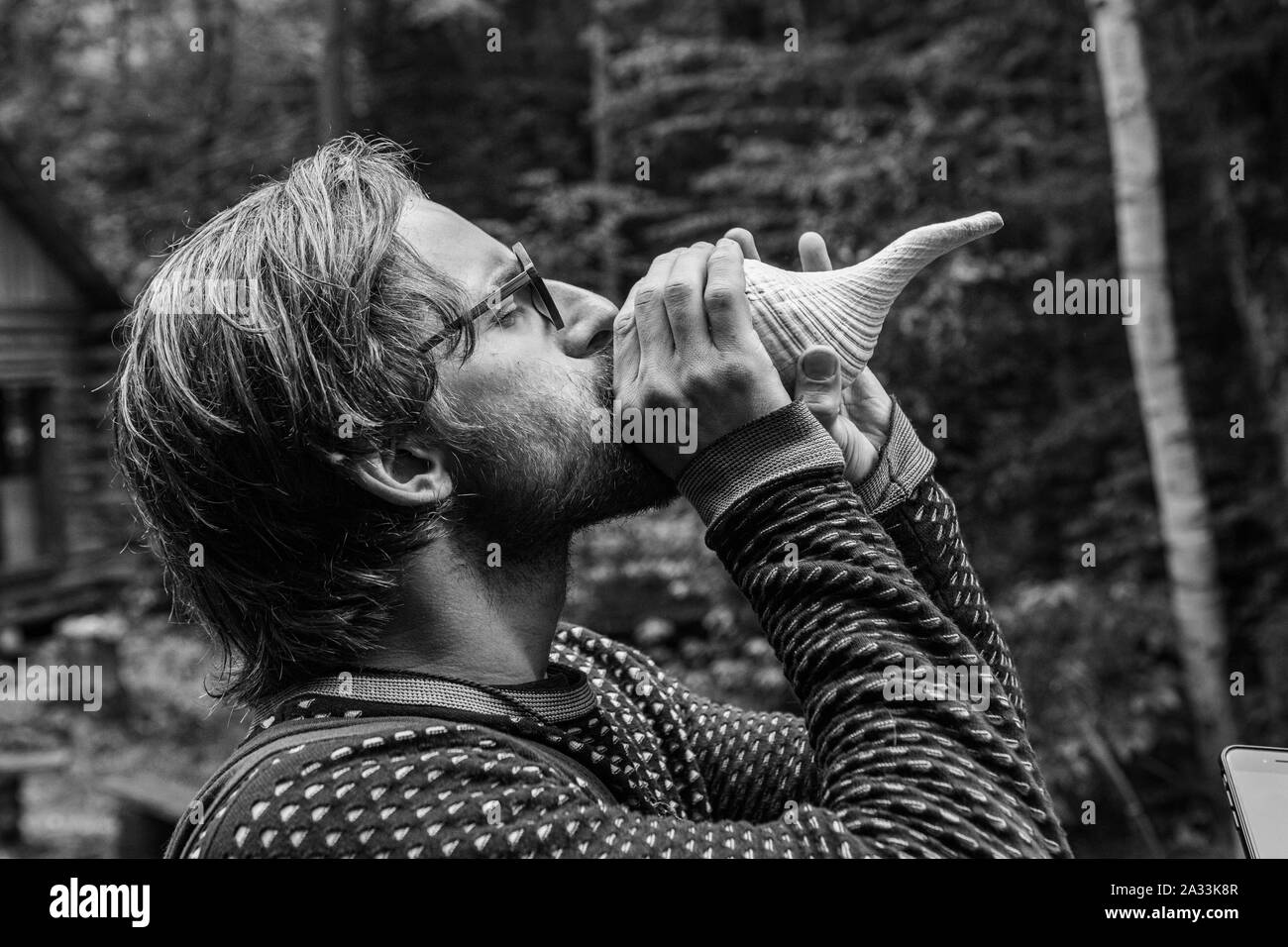 A monochrome view of a young shaman guy playing a sacred conch in ...